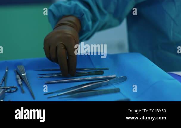 Hand on unrecognized medic in brown latex glove moving the metal tools at the surgical stand ...