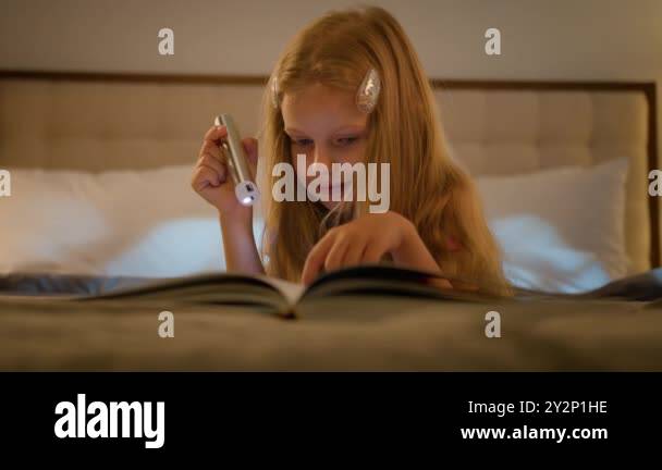 Curious Caucasian child little girl reading book instructive story textbook daughter lying bed ...