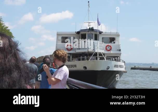 A white and blue ferry boat docked at a pier with a city skyline. The ...