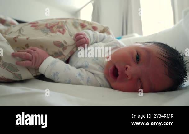 Newborn baby resting under a floral blanket, grimacing and gesturing as ...