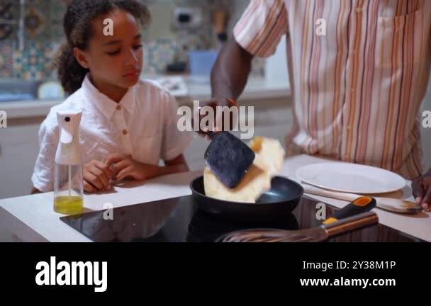 African American father man hand frying pancakes together with daughter ...