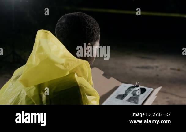 African American male detective in yellow raincoat squatting by ...