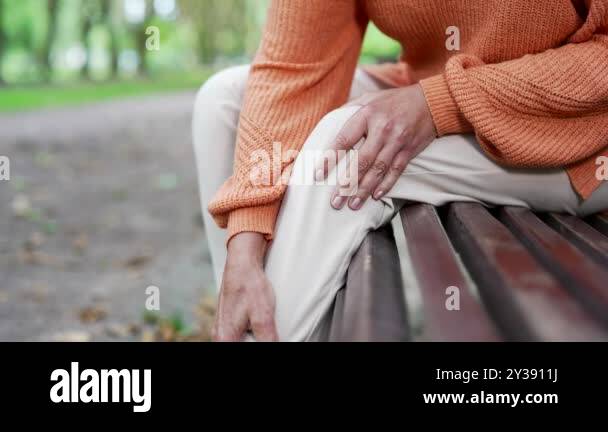 Elderly female hands massaging knee leg muscles while sitting on bench ...