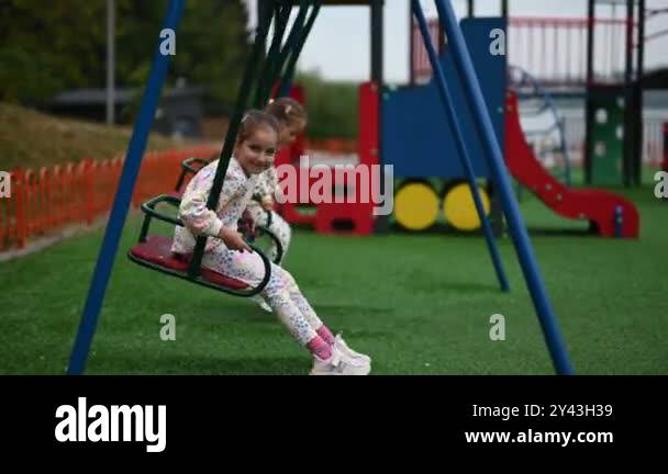 Two young sisters are having fun on the swings at a playground. They ...