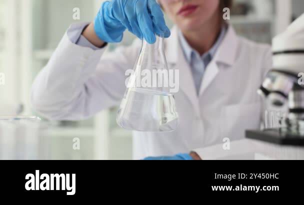 Female lab assistant shakes transparent liquid in conical flask at ...