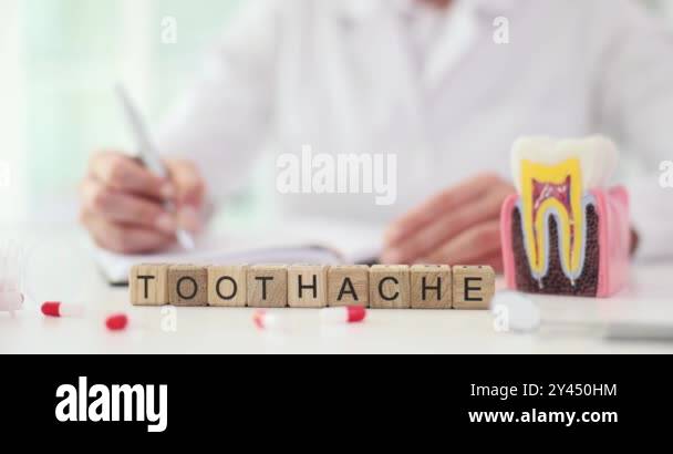 Cubes with word Toothache near tooth model against doctor writing notes ...