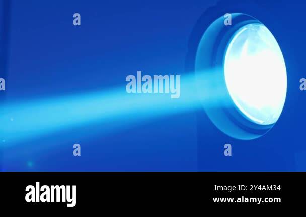 A powerful blue spotlight illuminates a dark space, creating a dramatic ...