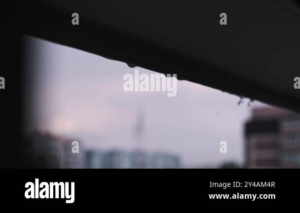 Close-up slow motion of raindrops falling from a window frame, creating ...