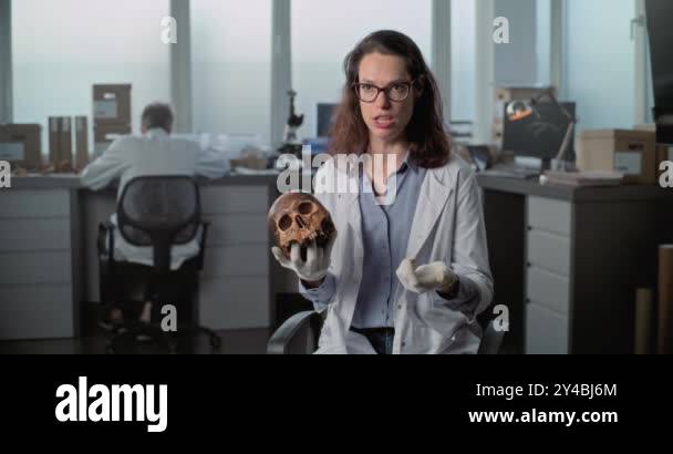 Female scientist speaks to camera, shows fossil skull of prehistoric ...