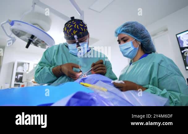 Male surgeon wearing a headlight shoves a long metal tool into the ...