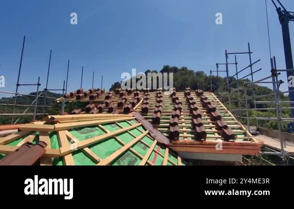 The photograph shows the ongoing construction of a residential roof, focusing on tiling work ...
