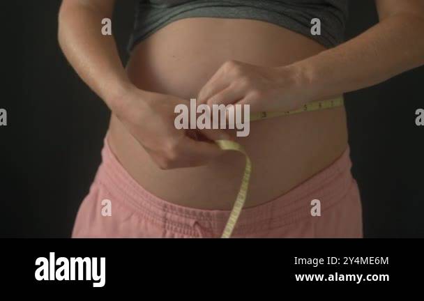 A close-up shot of a pregnant woman measuring her belly with a tape ...