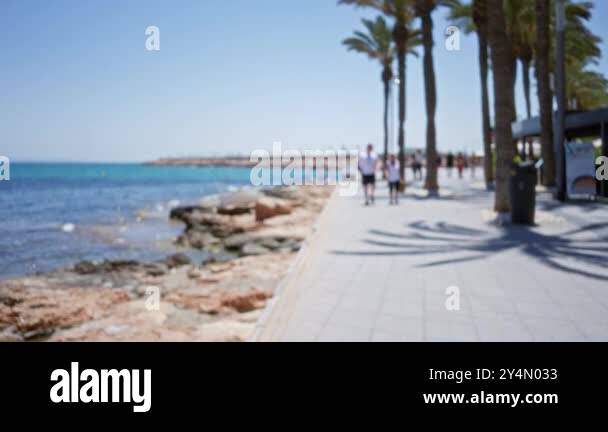 Outdoor scene of beach promenade with blurred people walking under palm ...