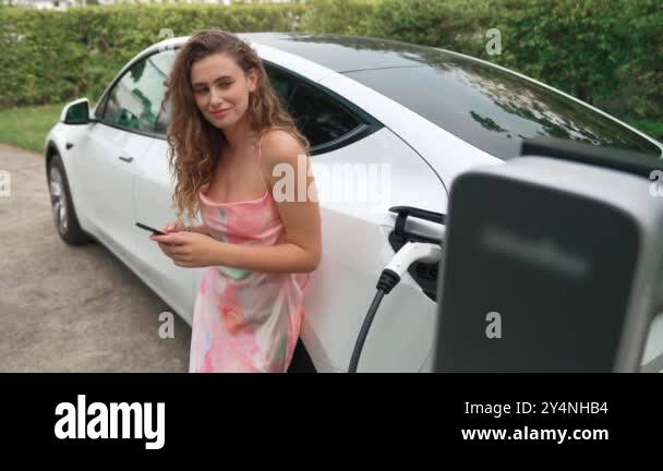 Modern eco-friendly woman recharging electric vehicle from home EV charging station. Innovative ...