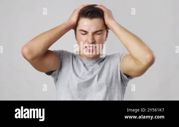 Weather dependence. Young man suffering from headache attack, rubbing his aching head, grey ...