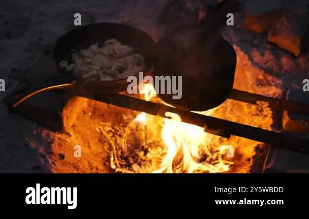 Under a starry night sky, a rustic campfire illuminates a blackened ...