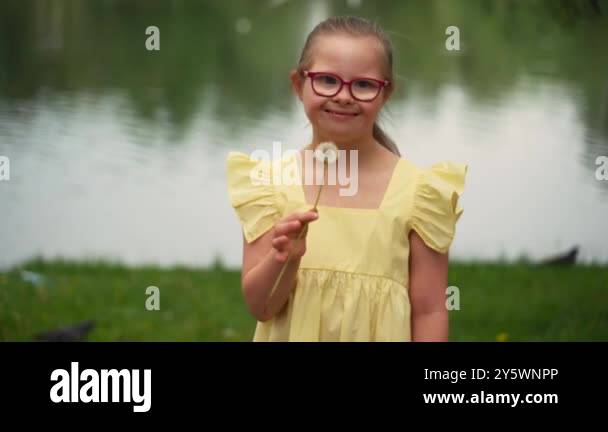 Young girl with Down syndrome in yellow dress is holding dandelion and ...