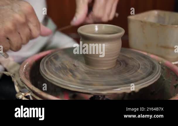A close-up of a potter's hand cutting off a finished clay jug from the ...
