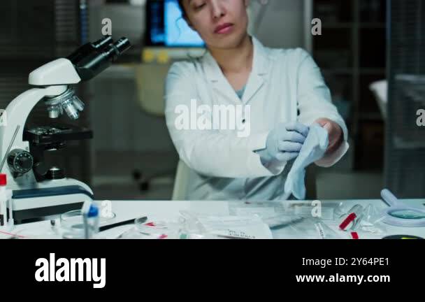 Tilt up shot of female forensic scientist putting on disposable gloves ...