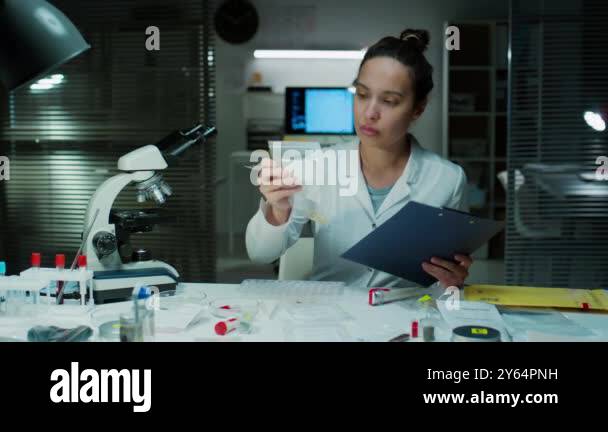 Female forensic scientist analysing bullet in evidence bag and taking ...
