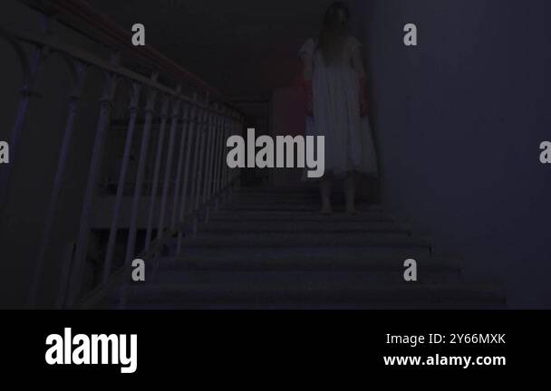 Young female on stairway in darkness. Creepy ghost woman in white dress ...
