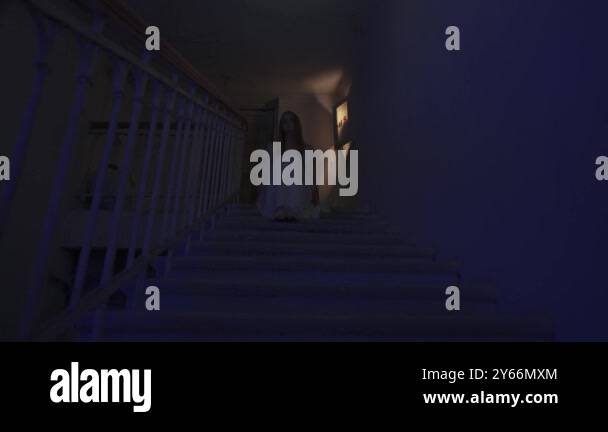 Young female on stairway in darkness. Creepy ghost woman in white dress ...