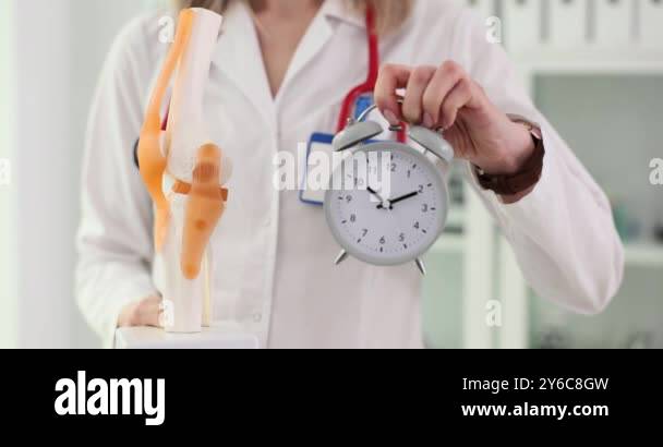 Doctor holds model of knee joint and alarm clock in clinic. Time and ...