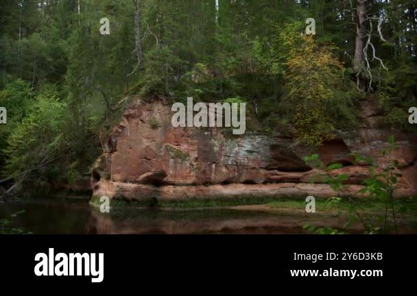Red Wild Rocks on the Steep Bank of a River with a Flowing Stream. The ...