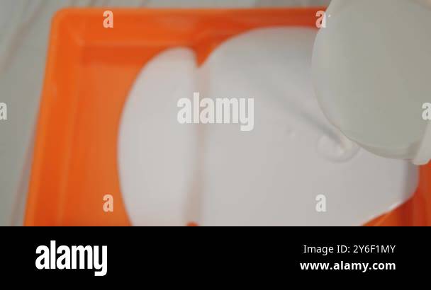 Close-up of white acrylic paint for walls inside a house being poured ...
