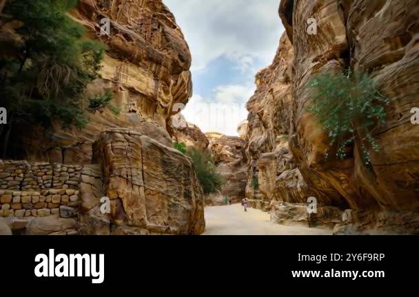 A narrow canyon path surrounded by towering, textured rock formations ...