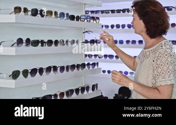 Sunglasses shopping, woman trying on frames, surrounded by different styles, modern interior ...