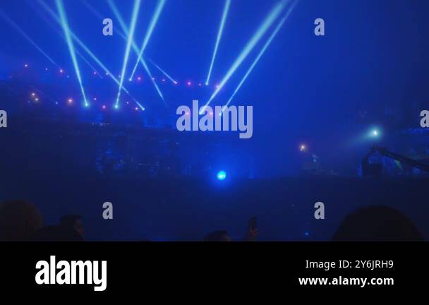 A concert scene shrouded in blue fog, featuring bright beams of light ...