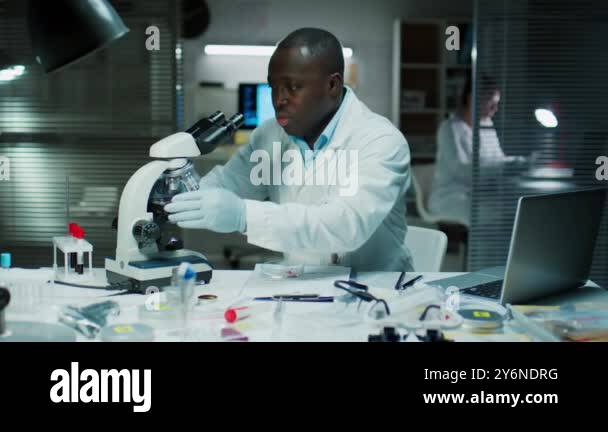 Black forensic scientist examining evidence under microscope and taking ...