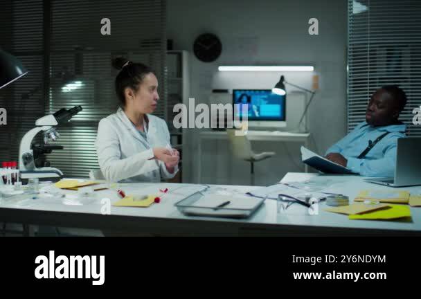 Female forensic scientist sitting at desk in crime lab and describing ...