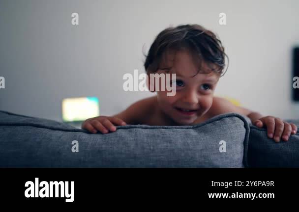 Smiling child peeking over the back of a couch, exuding playful energy ...