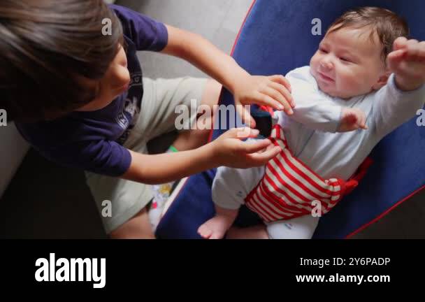 Older sibling interacting with baby in a chair, sharing a playful ...