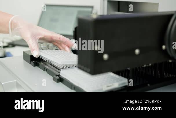 Laboratory technician wearing gloves placing microplate into automated machine for scientific ...