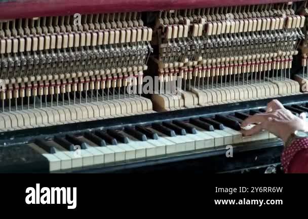 A close-up of a hand playing an old piano, showing the internal hammers ...