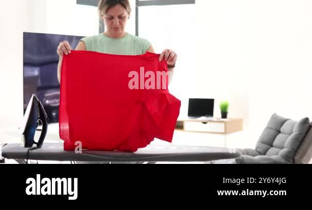 Woman irons red silk shirt on ironing board. Ironing clothes on ironing ...