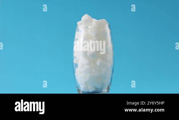 Transparent glass full of cubes of white sugar stands on bright blue ...