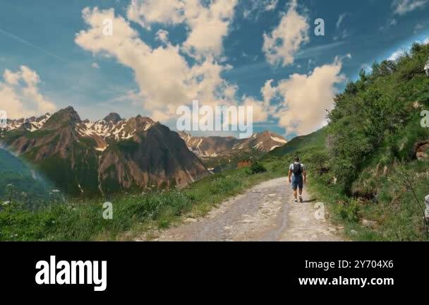 A lone hiker with a backpack walks along a scenic mountain trail ...