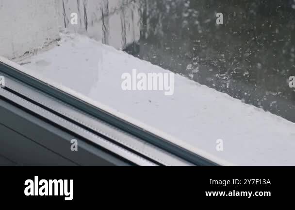 Close-up footage of rain streaming down a window pane and pooling on the window sill, blurring ...
