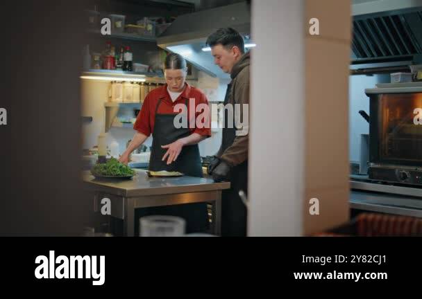 Two chefs discussing food preparation in professional kitchen workspace ...