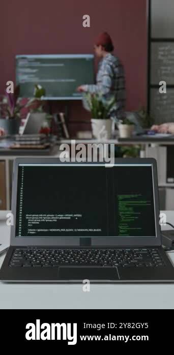 Vertical timelapse of laptop on desk in IT company, lines of code running on black screen. Team ...