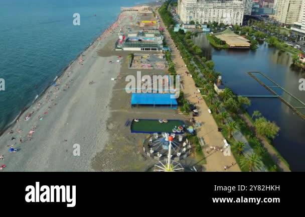 Amusement park rides slowly spin on crowded beach, and tourists enjoy ...