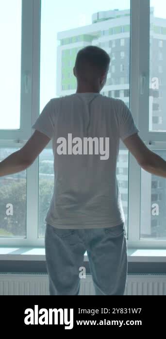 Early morning, a man at the window raising his hands and stretching ...