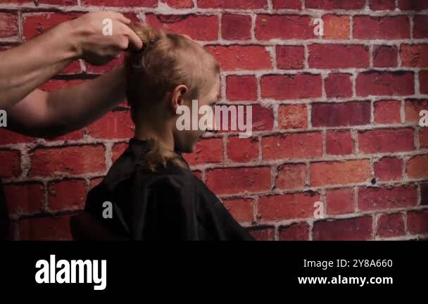 Using a hair clipper, the barber does the boy's hair. A teenage boy's ...
