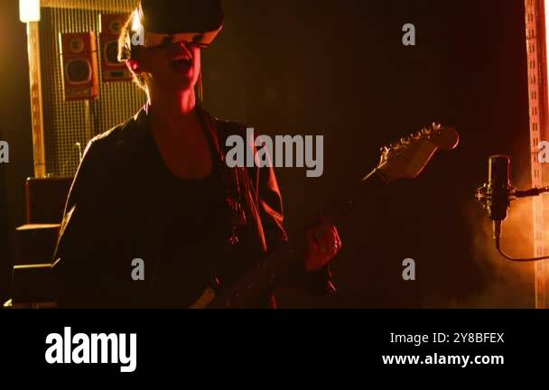 Confident trendy rocker girl playing guitar with vr glasses on her head ...