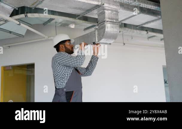 Indian worker installs a ventilation system in an office building. The ...