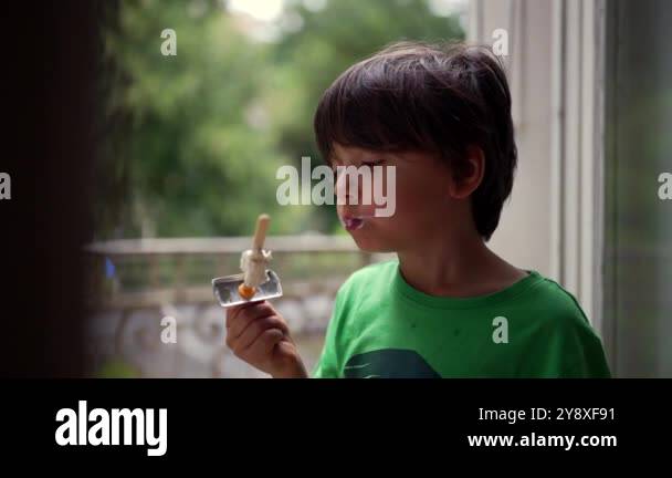 Young boy eating ice cream outdoors, biting into a popsicle while ...